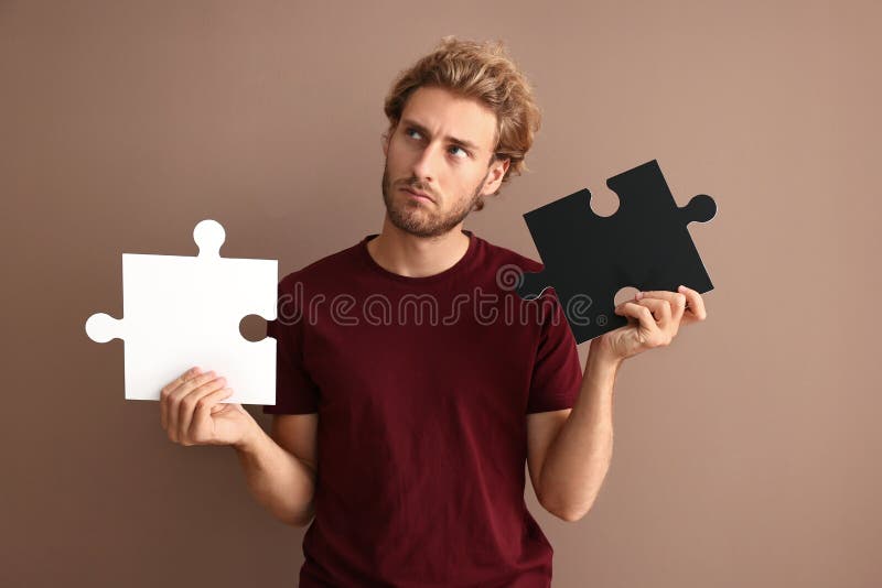Thoughtful Young Man with Pieces of Jigsaw Puzzle on Color Background ...