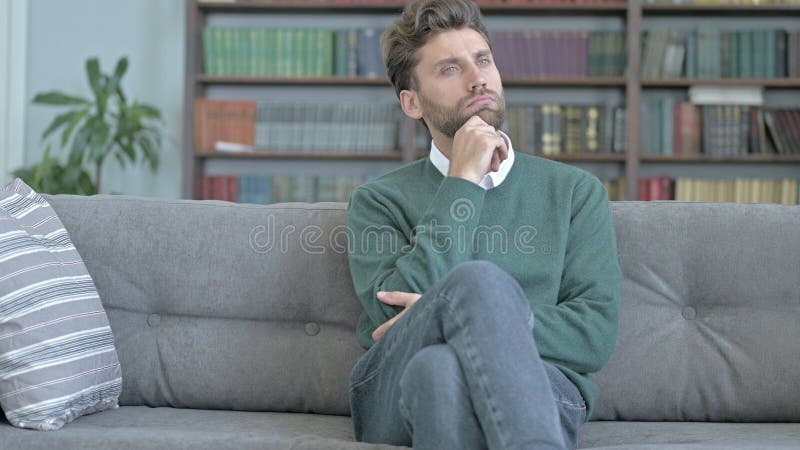 Thoughtful Young Man Sitting on Sofa while Thinking about Something ...