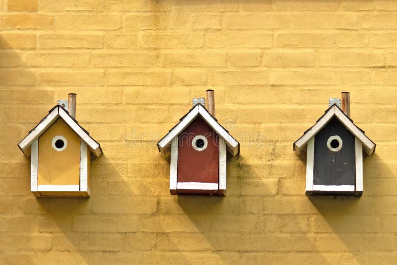 Three Bird Nesting Boxes in Different Colors Hanging on a Yellow House ...