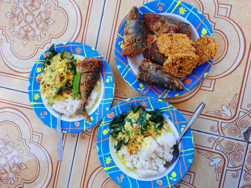 Three Blue Plates Hold Rice, Fried Fish, Tempeh, and Spinach in Yellow ...