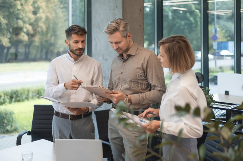 Three Business People Discussing Work Together Using a Tablet and ...