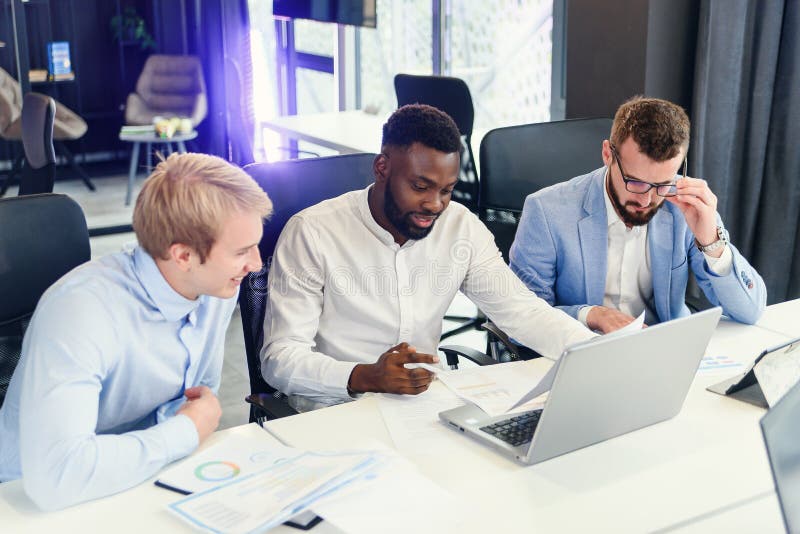 Three Businessmen Sitting at the Modern Office Tables and Analysing ...