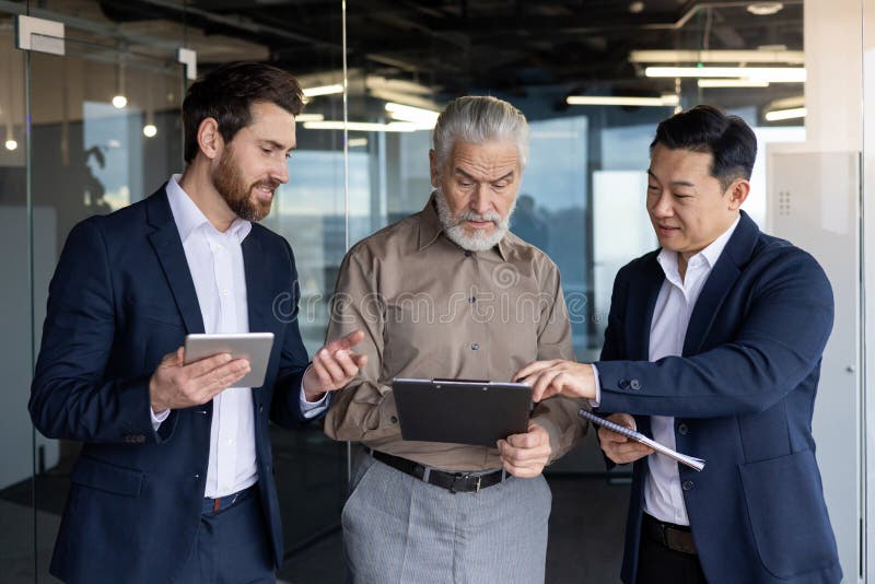 Three Businessmen in Suits Stand in the Office with Tablets and ...