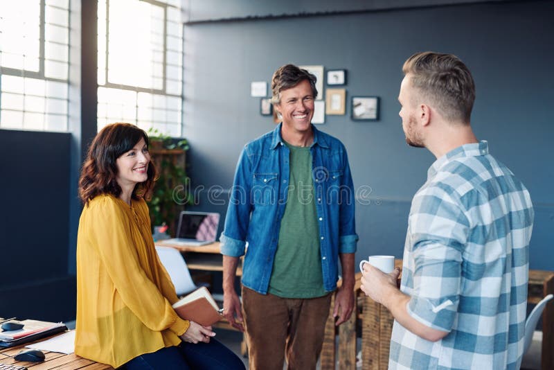Three Coworkers Smiling and Talking Together in a Modern Office Stock ...