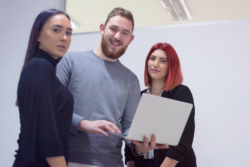 Three College Students Standing in Corridor and Using Laptop and ...