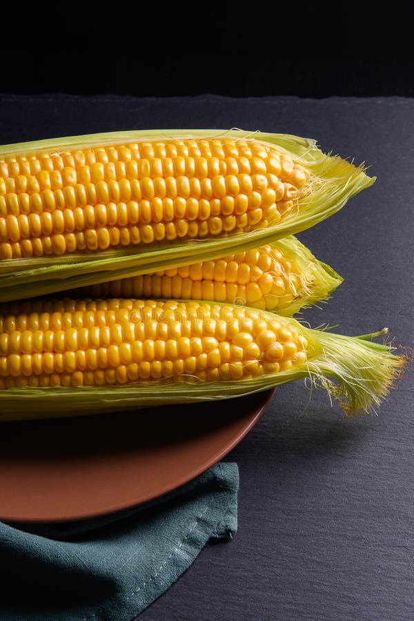 Three Corn Ears with Green Leaves and Plate on Dark Background Stock ...