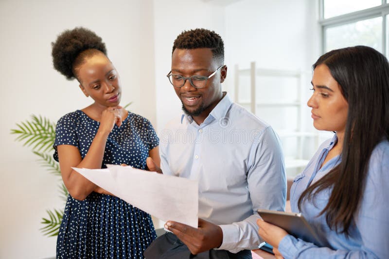 Three Coworkers Stand and Discuss Workplace Issues with Paper, Tablet ...