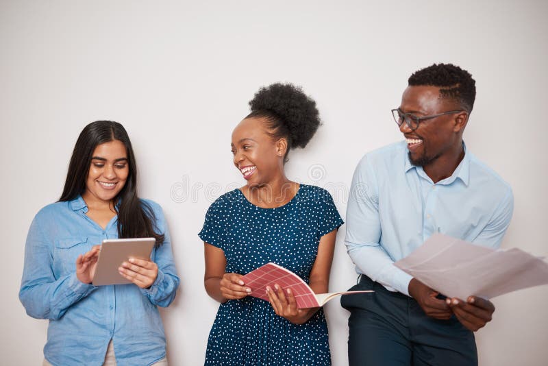 Three Diverse Colleagues Lean Against a Wall Sharing Notes and Reports ...