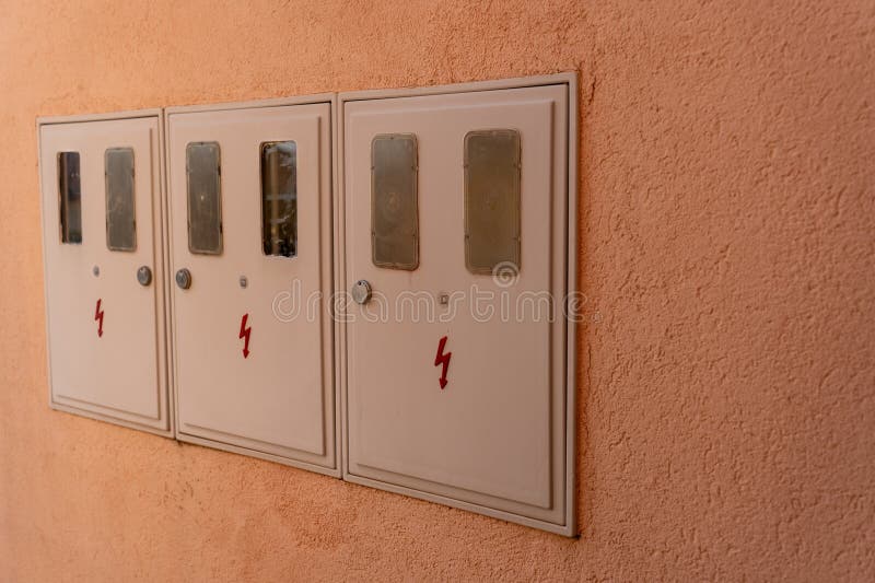 Three Electrical Meter Boxes with Warning Symbols on Textured Orange ...