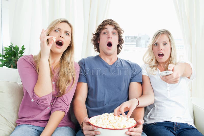 Three Friends Enjoying Popcorn Together while Shocked at the Tv Stock ...