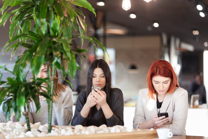 Three Friends Sitting at a Cafe Bar Looking at Phones Stock Image ...