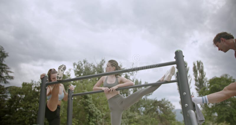 Friends Stretching Legs at Parallel Bars in Park: Fitness, Calisthenics, and Cloudy Day Workout ...