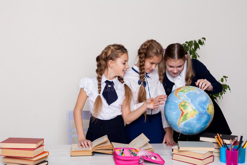 Three Girls of the School with Books for Studying Sit at the Desk in ...