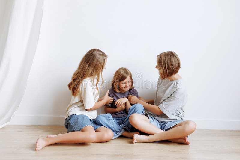 Three Girls Sisters Sitting On The Floor Against A White Wall Stock