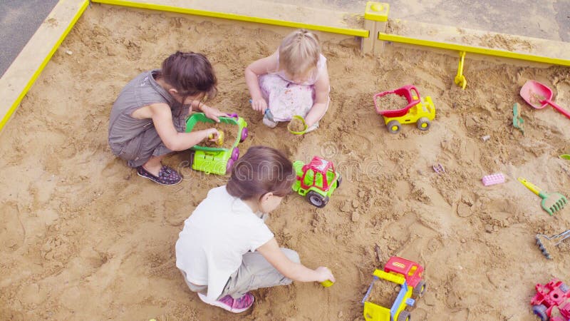 Three Girls Sitting in a Sandbox and Picking Up Sand Stock Photo ...