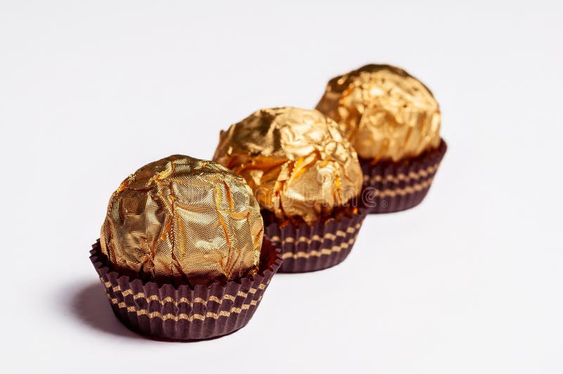 Three Golden Wrapped Hazelnut Chocolates in Brown Cups Sit Elegantly on ...