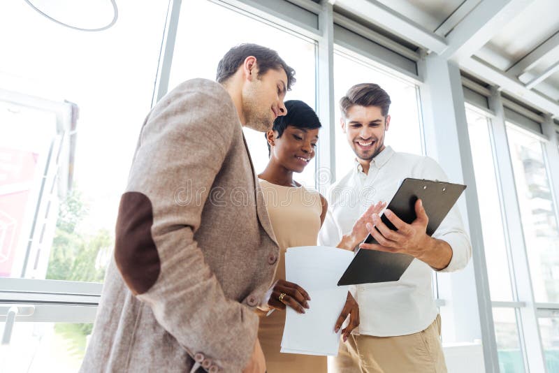 Three Happy Business People Looking through Documents Together in ...