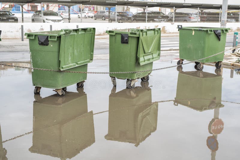 Three Large Green Plastic Waste Bins on Wheels Reflected in Rain Puddle ...