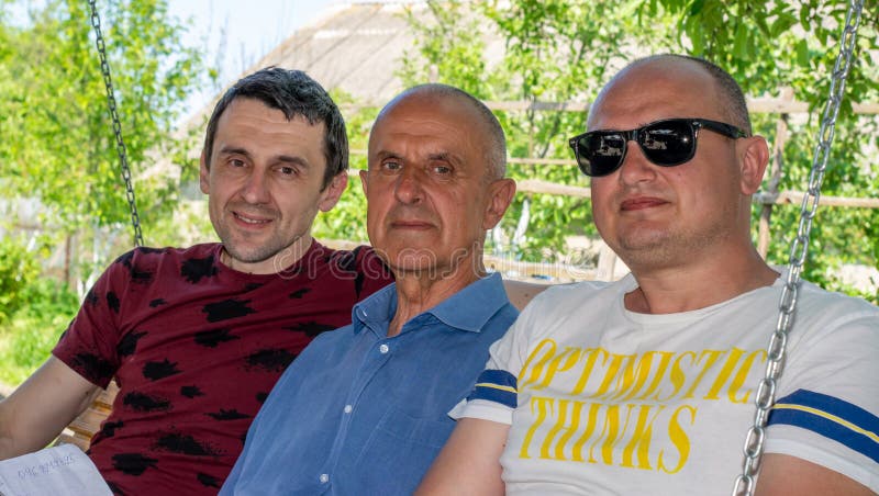 Three Men of Different Ages are Sitting on a Swing in the Garden. Stock ...