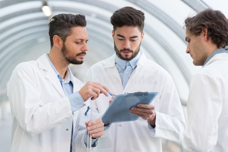 Three Men in Labcoats Looking at Clipboard Stock Photo - Image of ...
