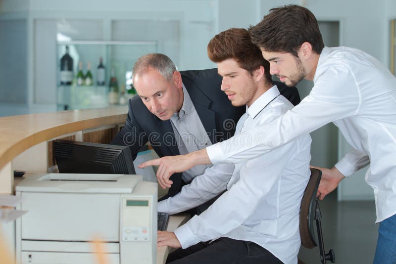 Three Men Looking at Computer Screen Behind Reception Desk Stock Image ...