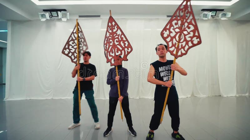 Three Men Practicing Traditional Dance with Large Ornate Props in a ...