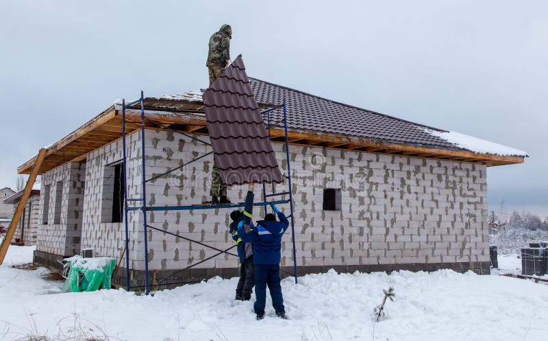 Three Men are Working on a House, One of Them is Holding a Piece of ...