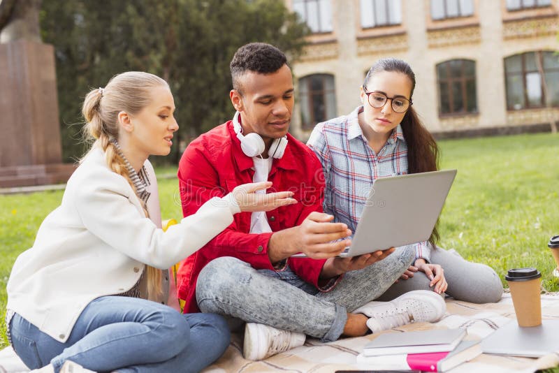 Three Millennials Shopping Online while Sitting on the Grass Stock ...