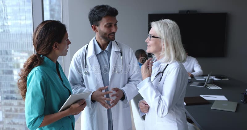 Three Multinational Medical Workers Talking Standing in in Clinic ...
