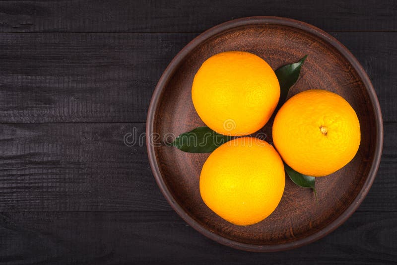 Three Oranges with Green Leaves Lie in a Brown Plate on a Brown Table ...