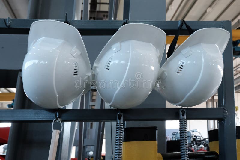 Three Protective White Helmets Hang on the Rack in the Factory. the ...
