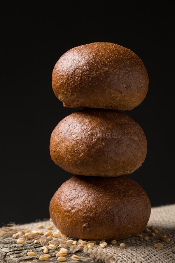 Three Rolls of Dark Bread on a Wooden Board with Wheat Grains, Black ...