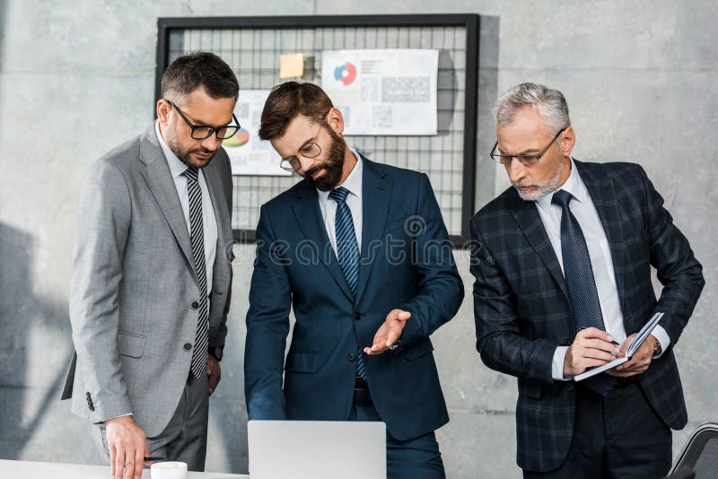 Three Serious Professional Businessmen Looking at Laptop and Discussing ...