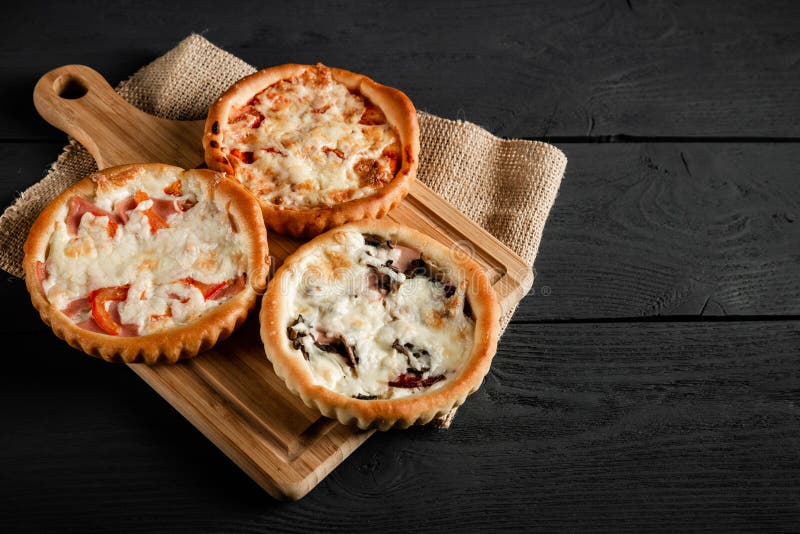Three Small Pizzas on a Cutting Board on a Black Wooden Background ...