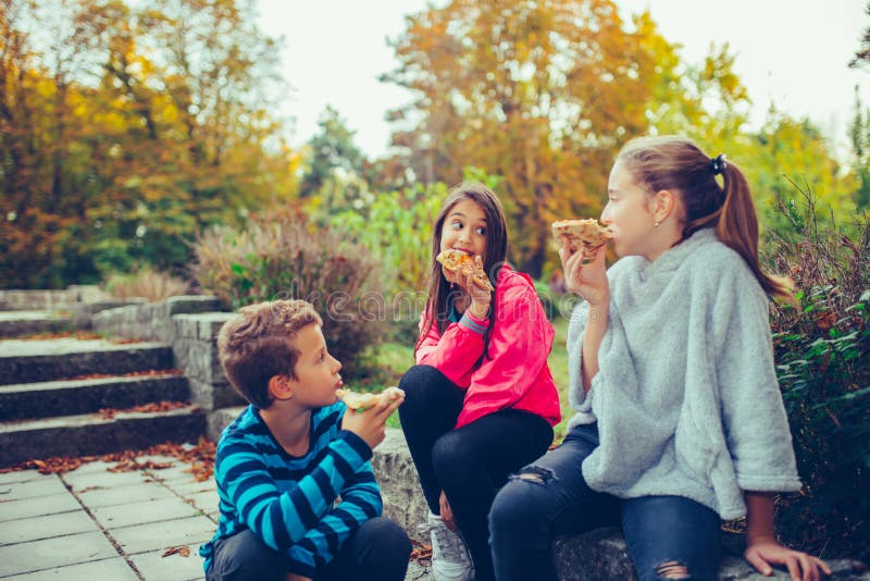 Three Smiling Children, Talking and Eating Pizza in the Park Stock ...