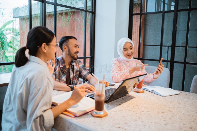 Three Smiling College Students Looking at Mobile Phone Screens Together ...