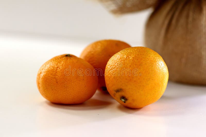 Three Tangerines on a White Table and a Brown Bag Behind Stock Photo ...