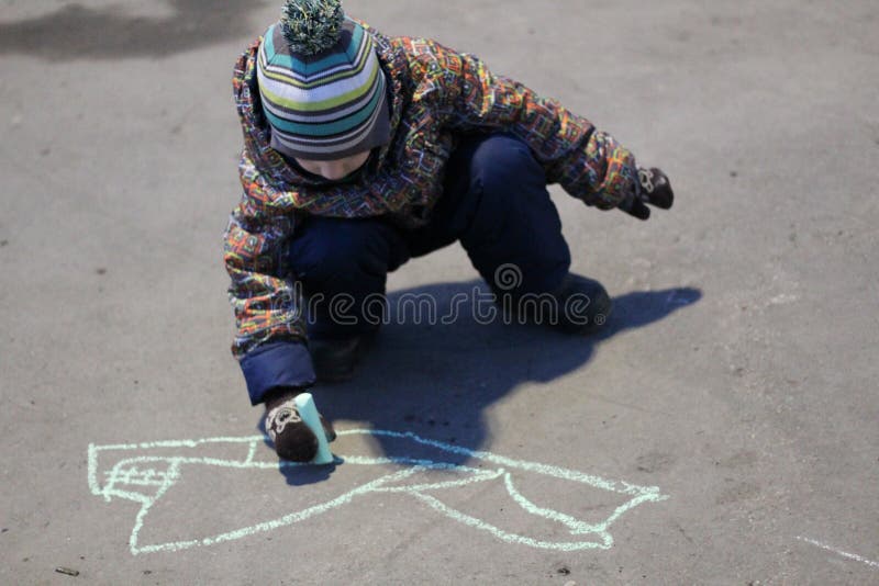 Three-year-old Boy in Colored Outerwear and Hat Draws Chalk on the ...
