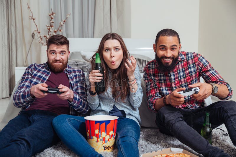 Three Young Friends Playing Computer Games and Drinking Beer Stock ...