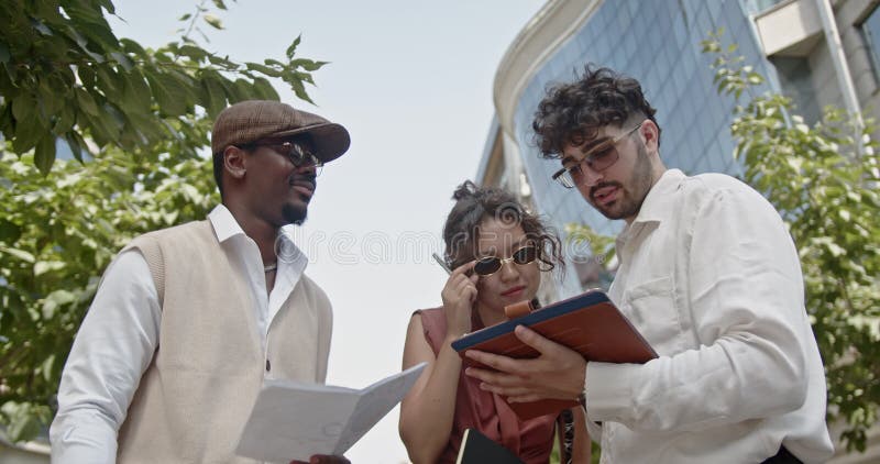 Three Young Professionals Collaborating on a Project Outdoors. they are ...