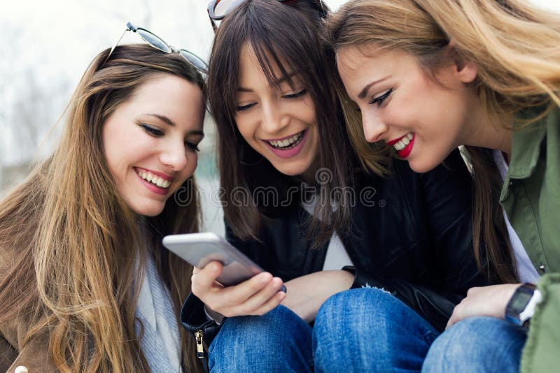 Three Young Women Using a Mobile Phone in the Street. Stock Photo ...