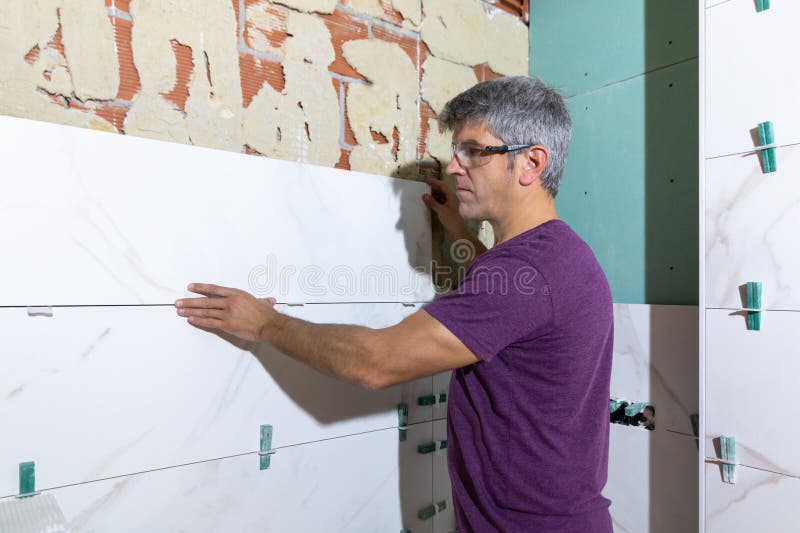 Tiler with Protective Glasses Placing a Piece of Large Format Tile on a ...