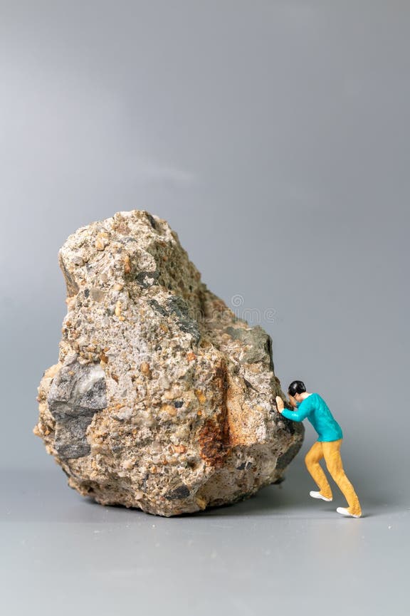 A Tiny Figurine of a Man Pushing a Massive Rock, Symbolizing ...