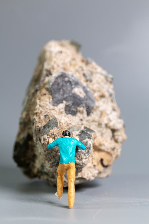 A Tiny Figurine of a Man Pushing a Massive Rock, Symbolizing ...