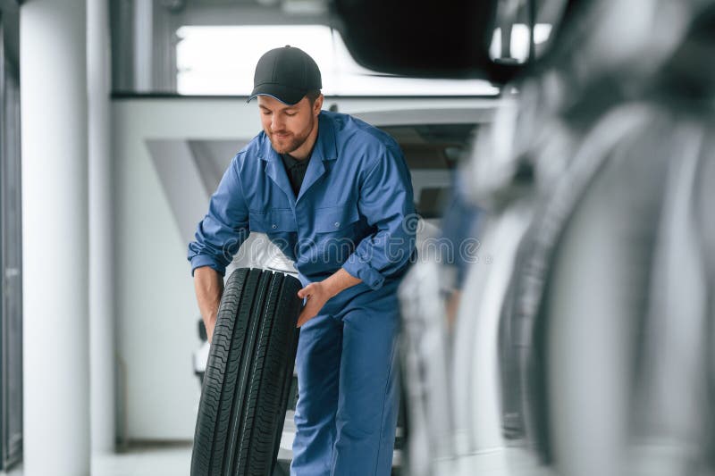 With Tire in the Hands. Man in Blue Uniform is Working in the Car ...