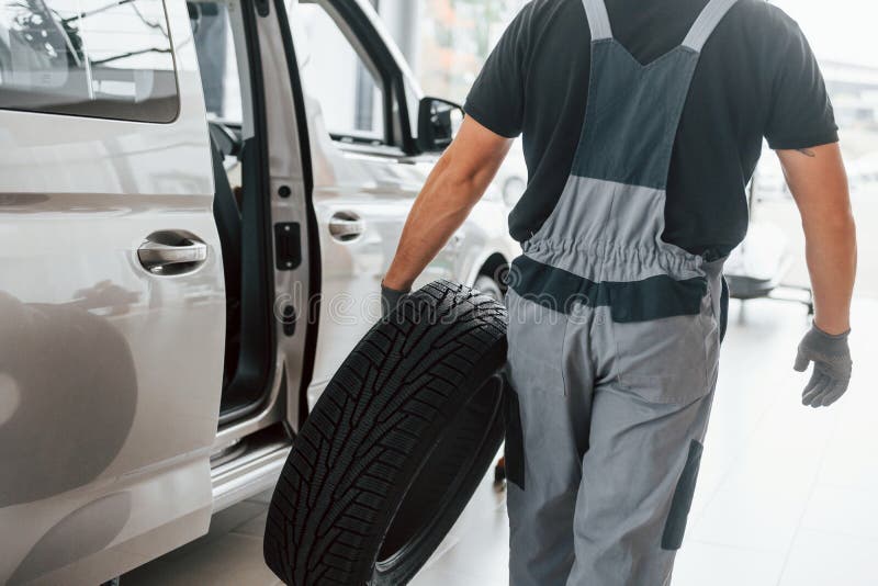 With Tire in Hands. Man in Uniform is Working in the Autosalon at ...