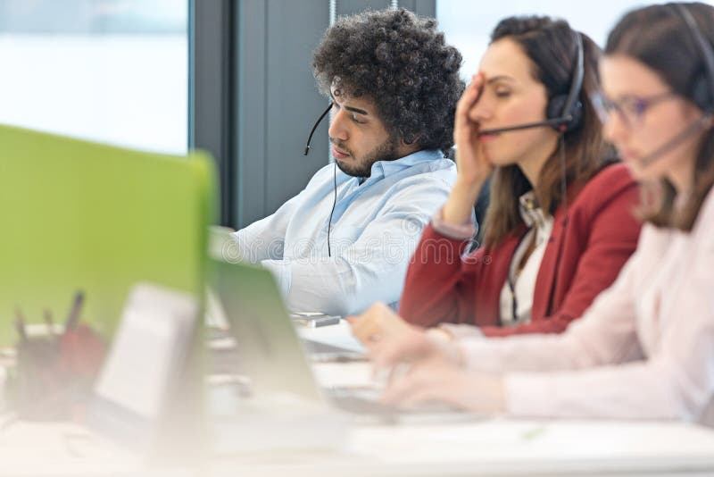 Tired Male Customer Service Representative With Colleagues Working In ...