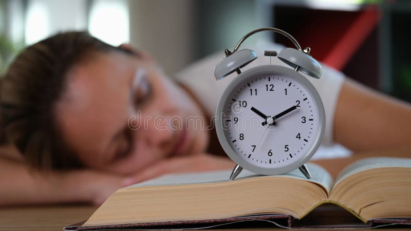 Tired Woman Sleeps on Table with Book and Alarm Clock. Stock Photo ...