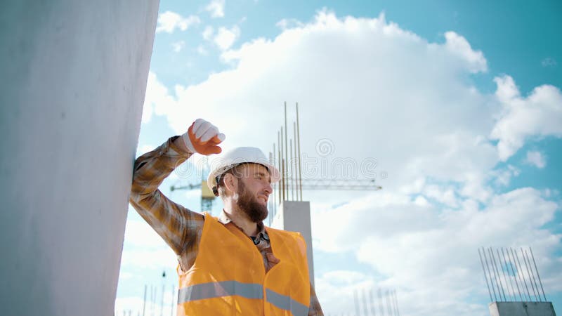 A Tired Worker at a Construction Site Rests His Hand on the Wall after ...