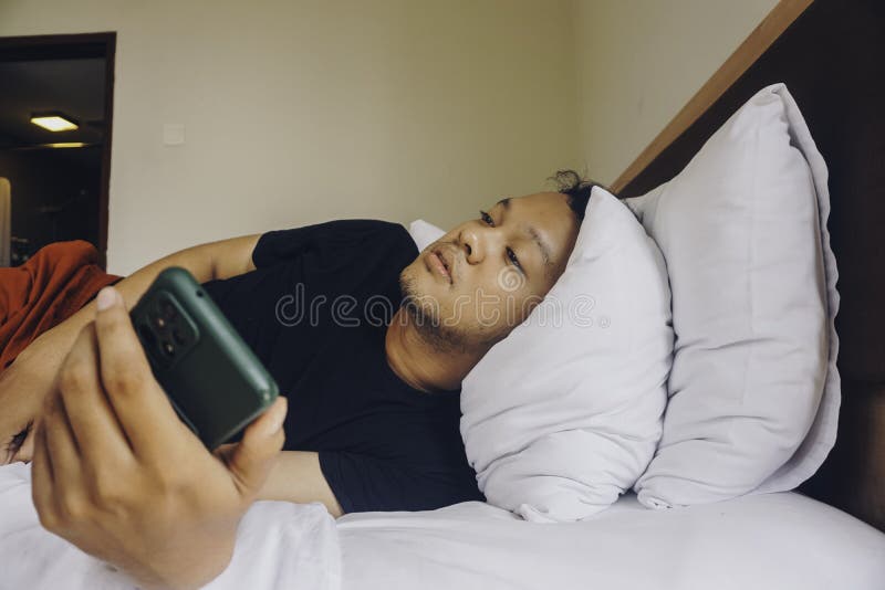 Tired Young Man Checking on His Phone while Lying in Bed Stock Image ...